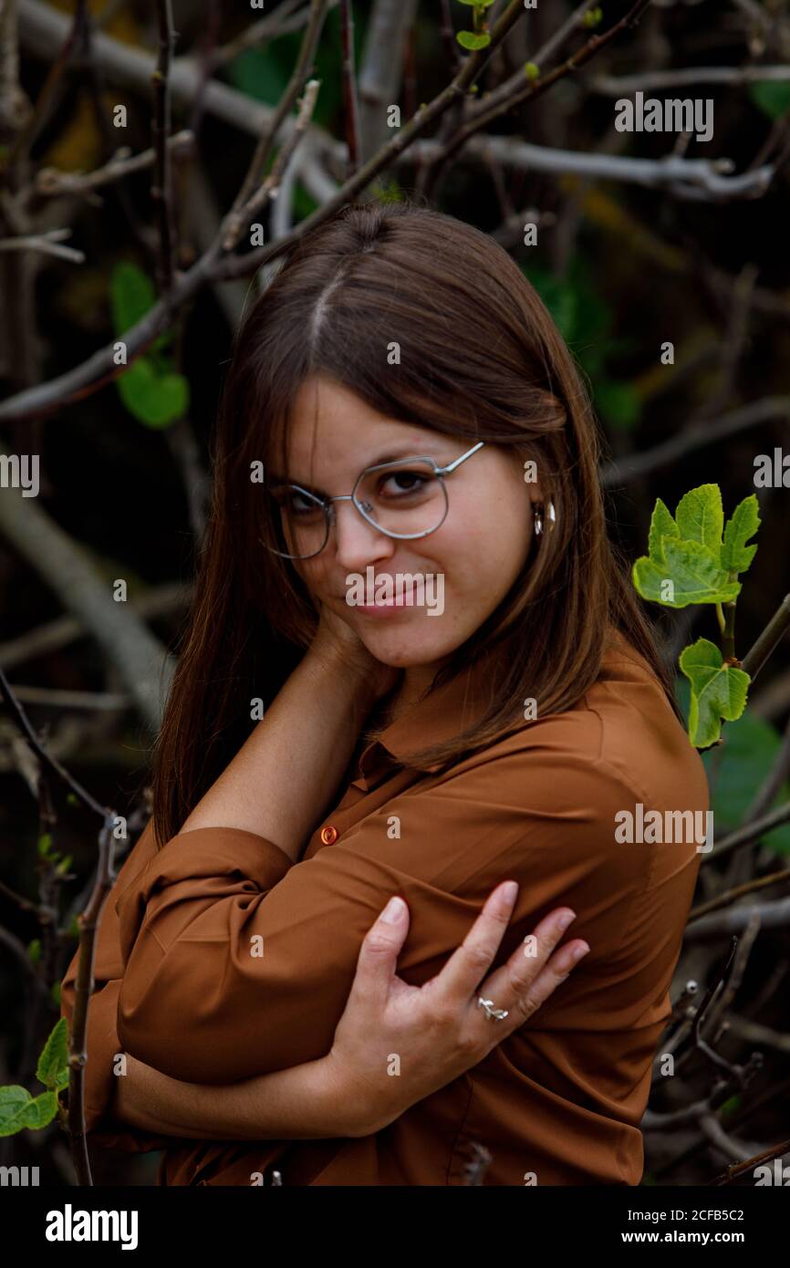 Side view of beautiful Woman standing in front of bushes looking at ...