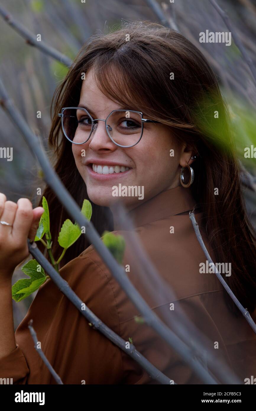 Side view of beautiful Woman standing in front of bushes looking at ...