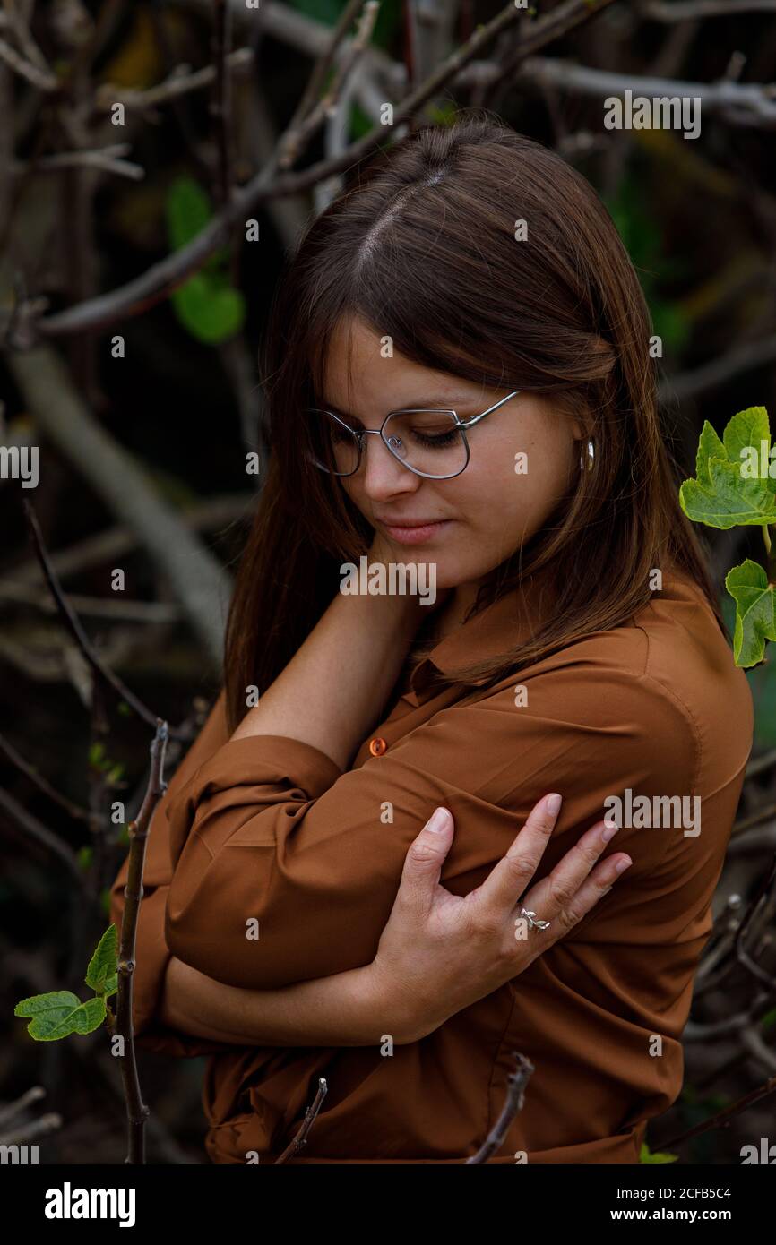 Side view of beautiful Woman standing in front of bushes looking down ...