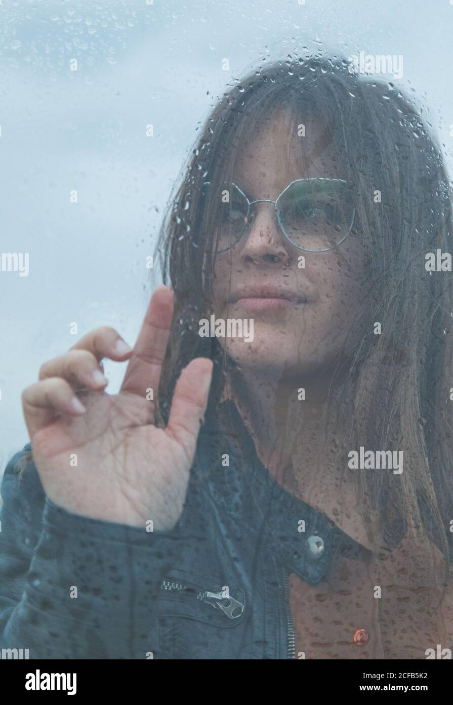 Portrait of beautiful Woman with glasses looking out of wet window on ...