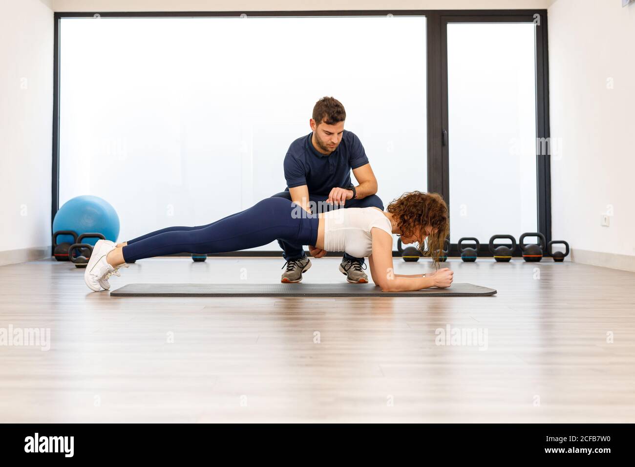 Side view of strong Woman in plank position with male personal trainer ...
