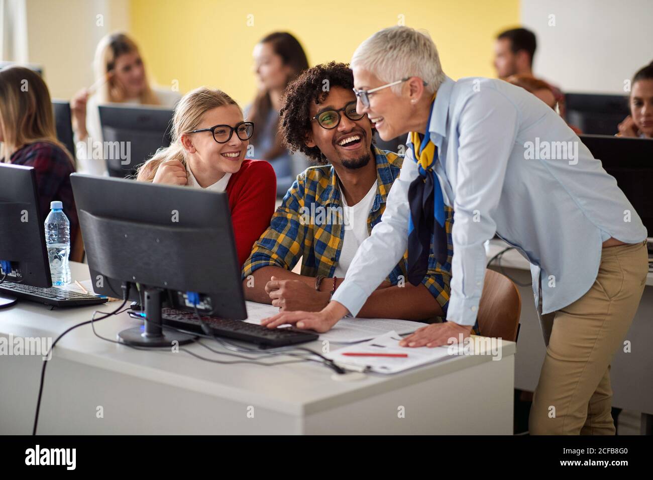 Female cheerful professor with pupils looking in computer Stock Photo ...