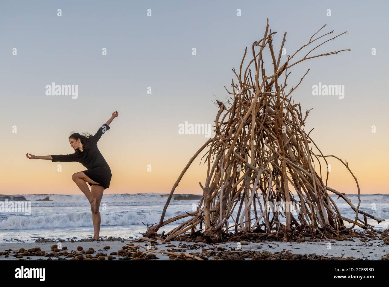 Young dancer on sand coast with wooden branches placed for campfire ...