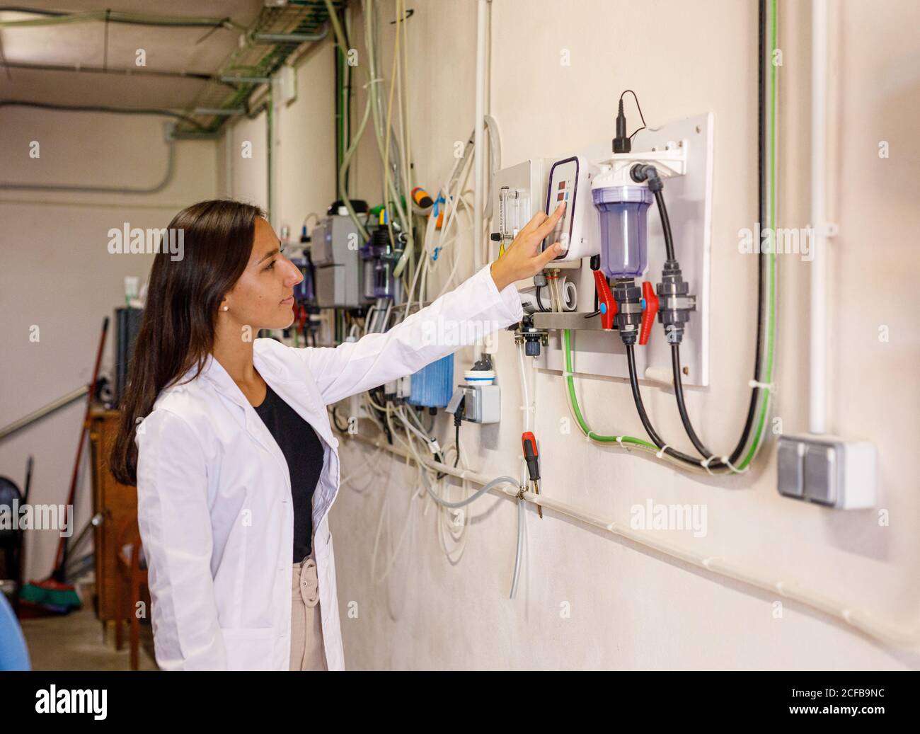 Side view of young female in lab coat pressing buttons on industrial ...