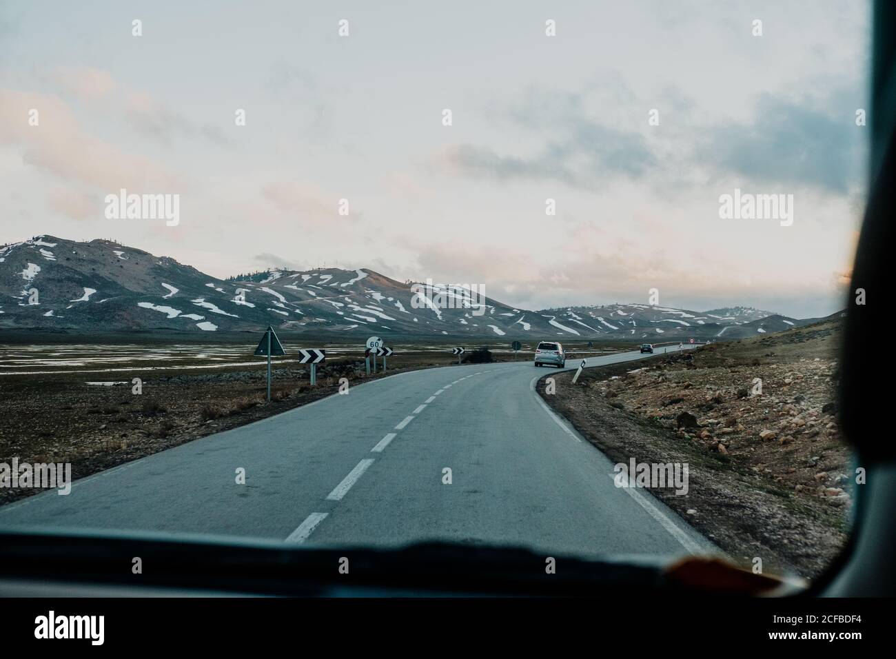 Asphalt road going through plains and hills in front of vehicle on gray ...
