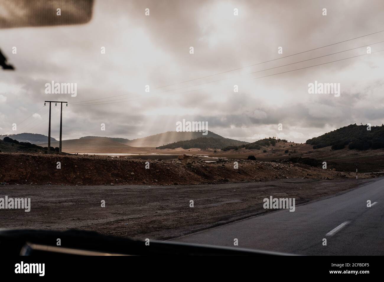 Asphalt road going through plains and hills in front of vehicle on gray ...