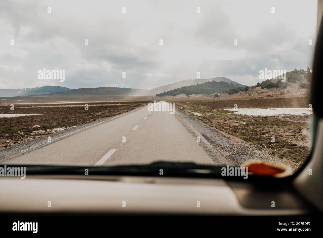 Asphalt road going through plains and hills in front of vehicle on gray ...
