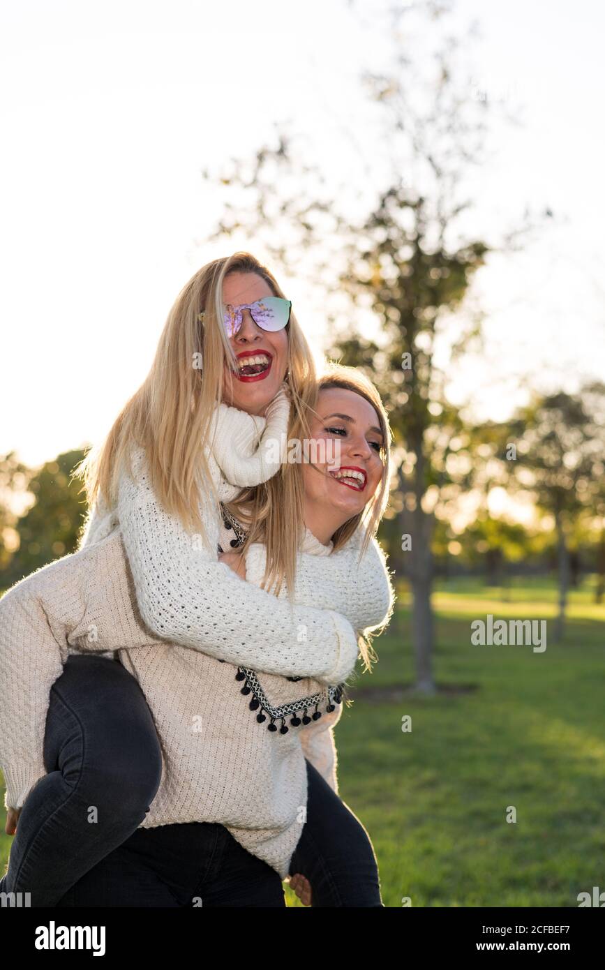 Blonde girl piggyback riding on her friend. Joking and smiling ...