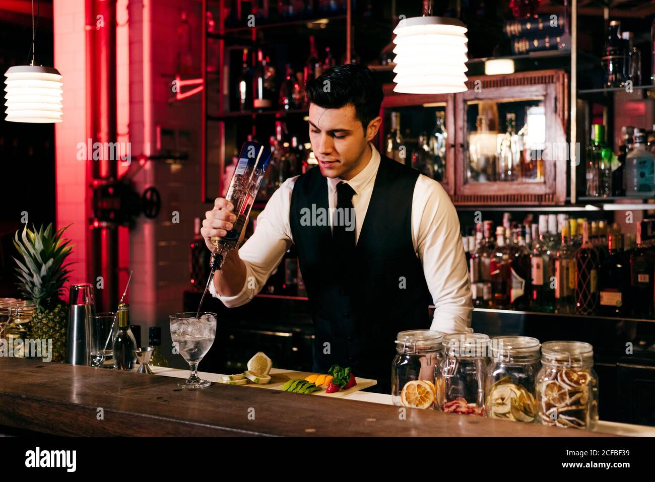 Young elegant barman working behind a bar counter mixing drinks with ...