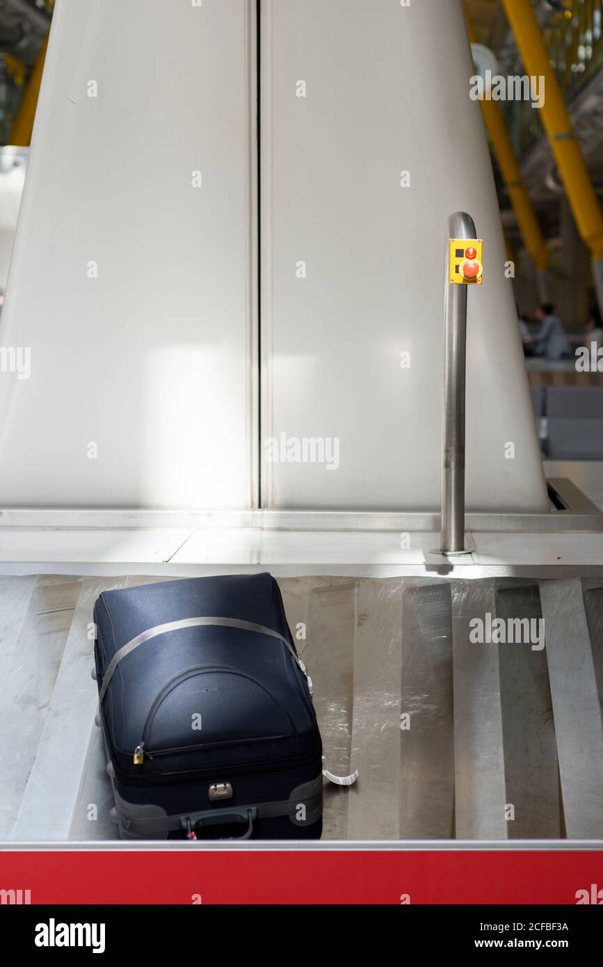 Metal baggage conveyor belt with suitcase near red emergency button at ...