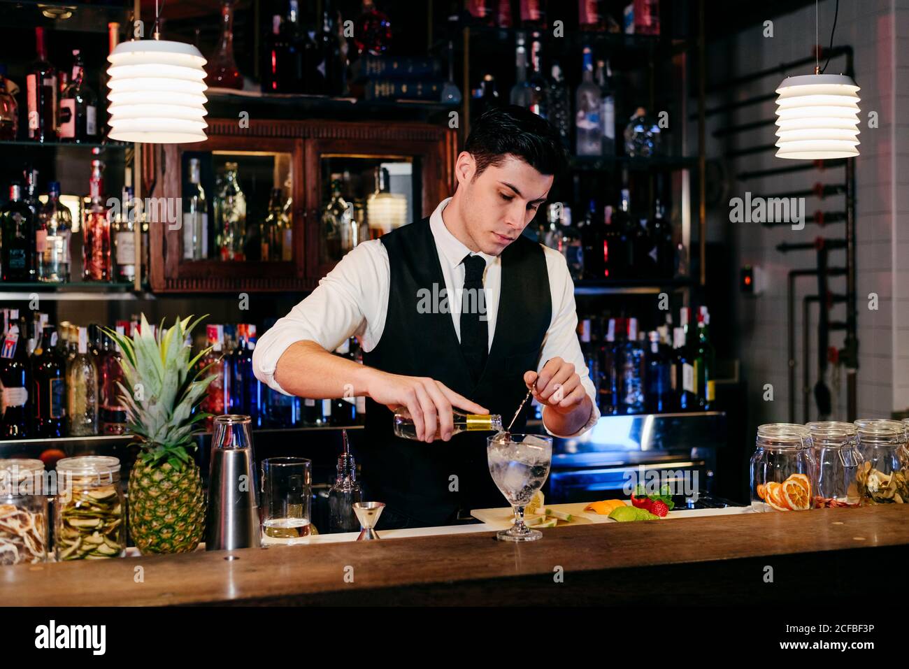 Young elegant barman working behind a bar counter mixing drinks with ...