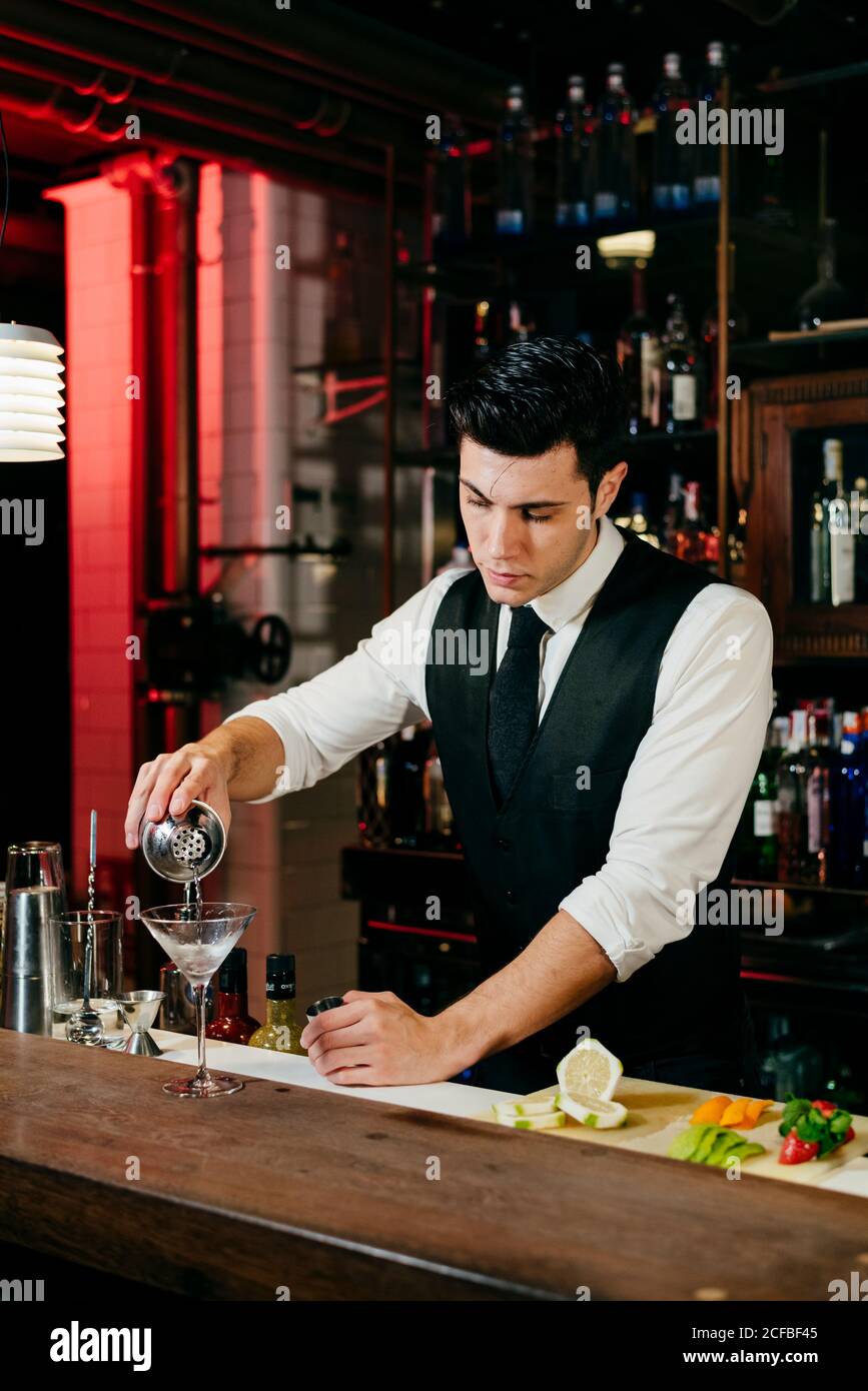 Young elegant barman working behind a bar counter mixing drinks with ...