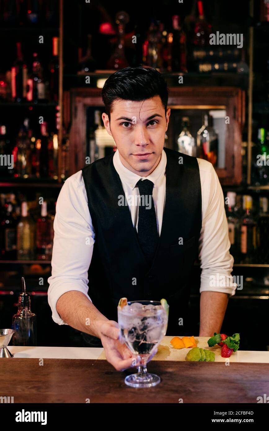 Young elegant barman working behind a bar counter mixing drinks with ...