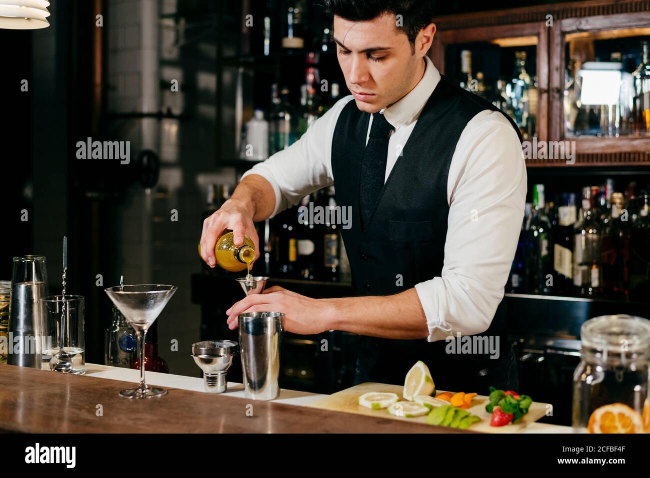 Young elegant barman working behind a bar counter mixing drinks with ...