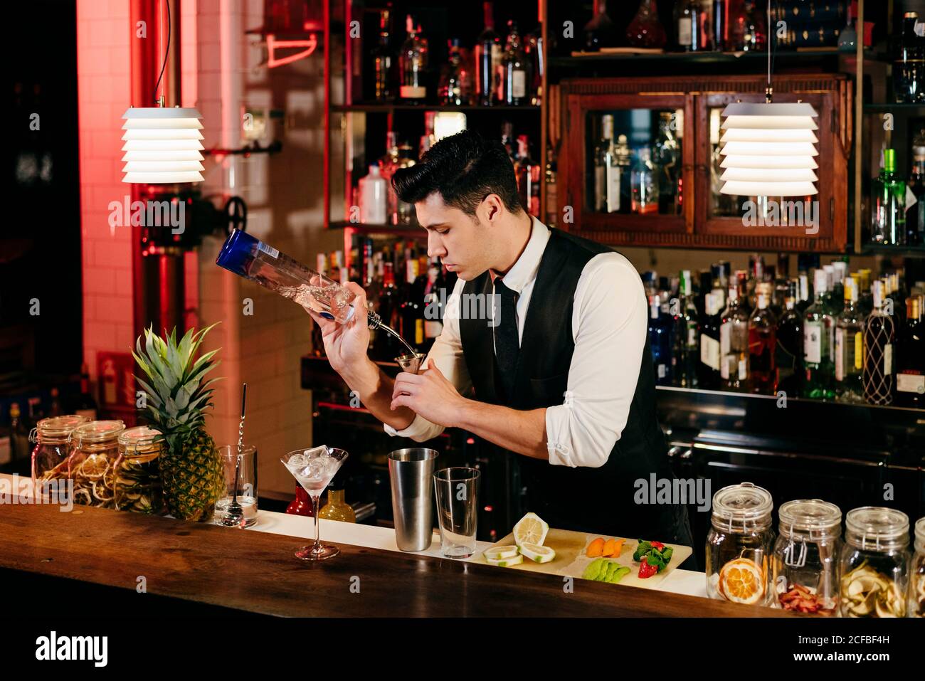 Young elegant barman working behind a bar counter mixing drinks with ...