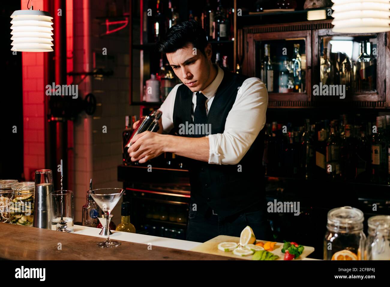 Young elegant barman working behind a bar counter mixing drinks in a ...