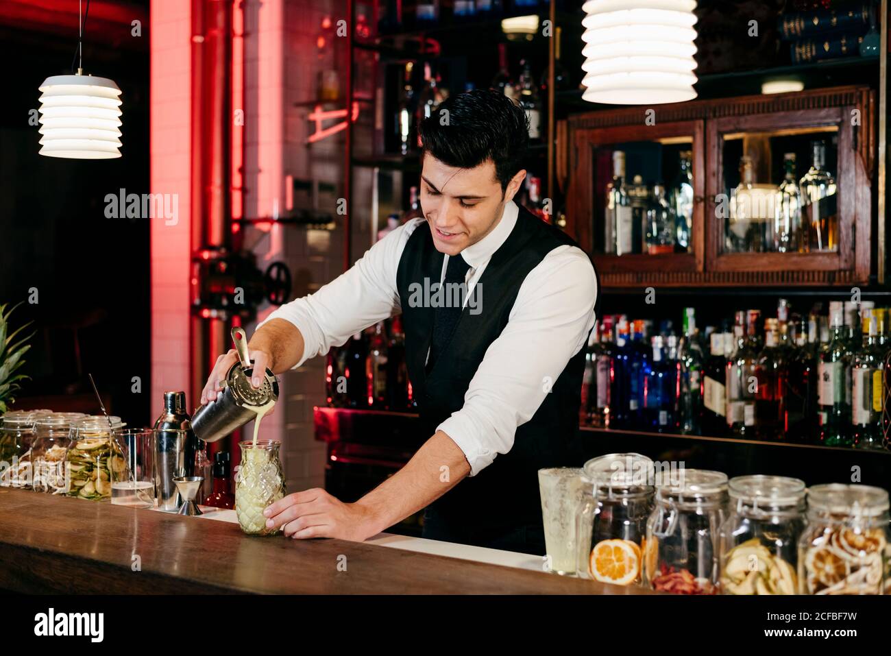 Young elegant barman working behind a bar counter pouring drink from ...