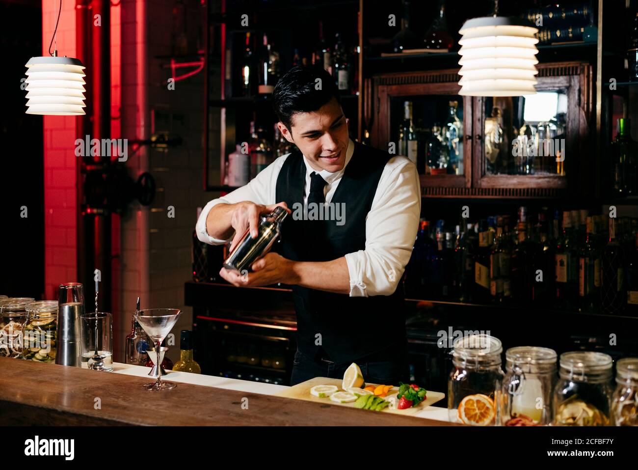 Young elegant barman working behind a bar counter mixing drinks in a ...