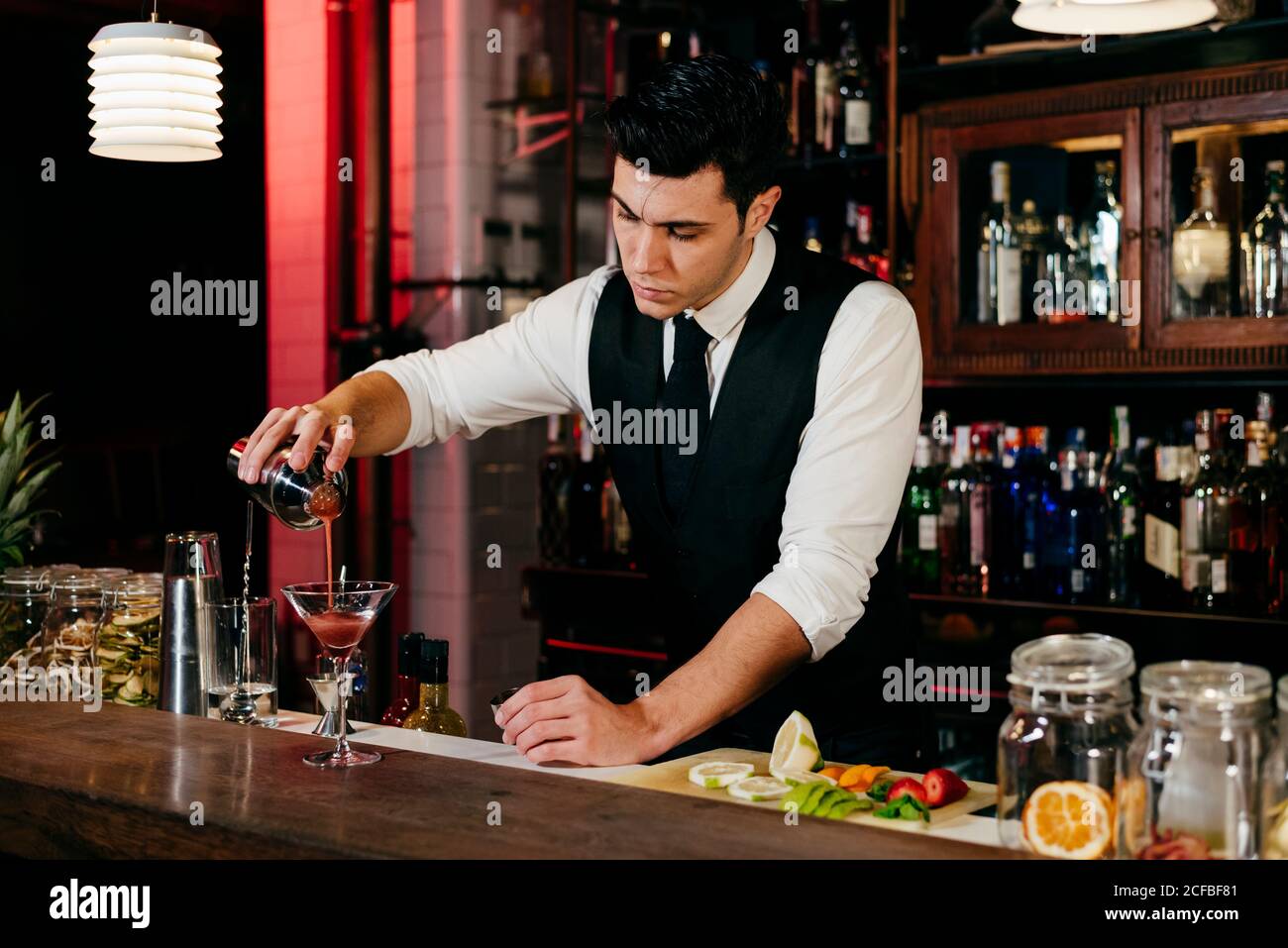 Young elegant barman working behind a bar counter pouring drink from ...