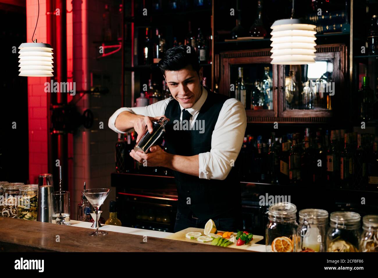 Young elegant barman working behind a bar counter mixing drinks in a ...