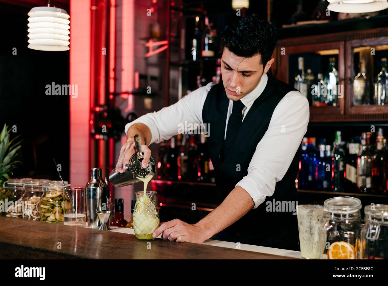 Young elegant barman working behind a bar counter pouring drink from ...