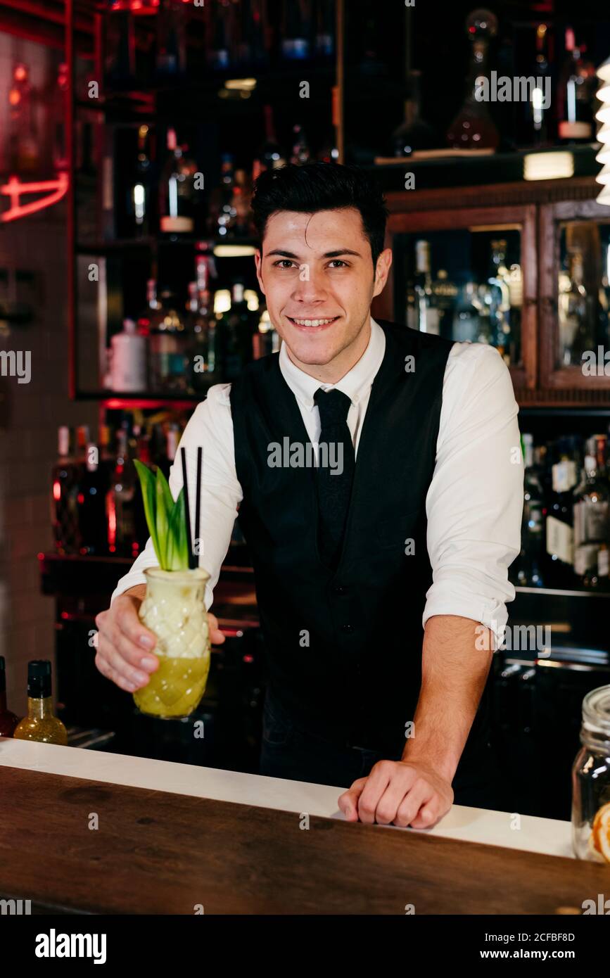 Young elegant barman working behind a bar counter preparing drink in a ...