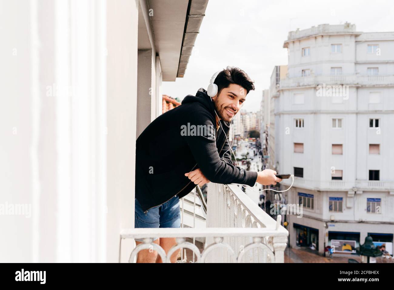 Young smiling handsome casual male in headset leaning on terrace ...