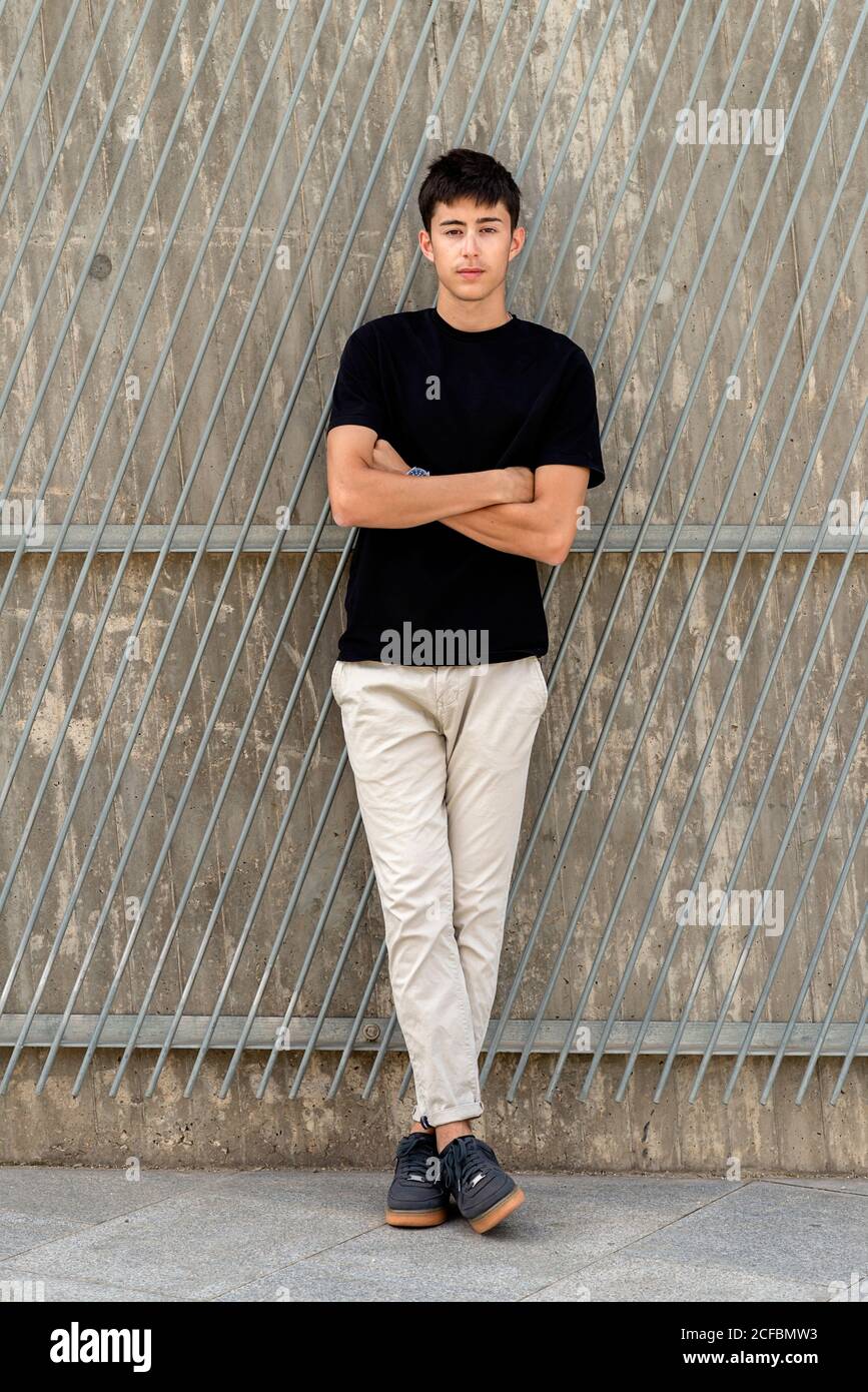 Young guy crossing arms leaning on wall, looking camera Stock Photo - Alamy