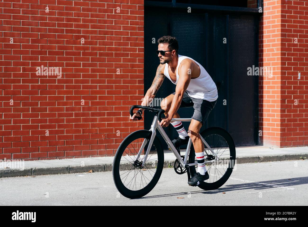 Modern male cyclist in sportswear and sunglasses riding a bicycle near ...