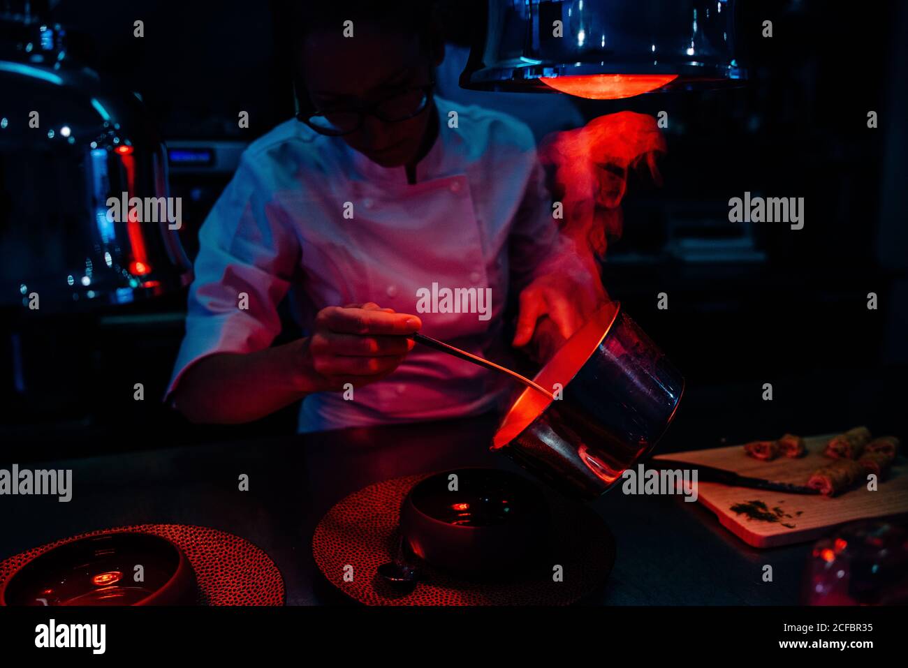 Female chef serving hot meal in restaurant kitchen with heat lamps ...