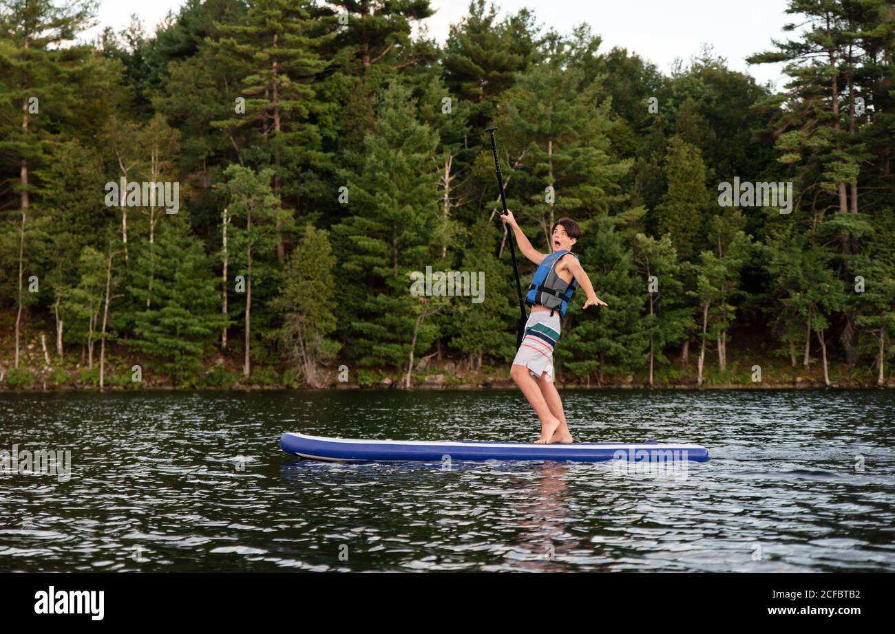 Teen boy falling off of a stand up paddle board (SUP) on a lake Stock ...