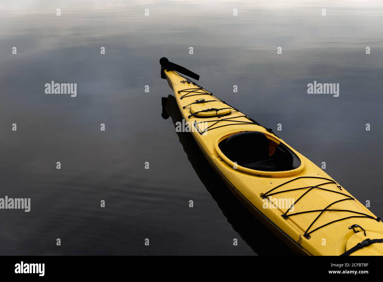 Bright yellow empty ocean kayak resting on calm dark water Stock Photo ...