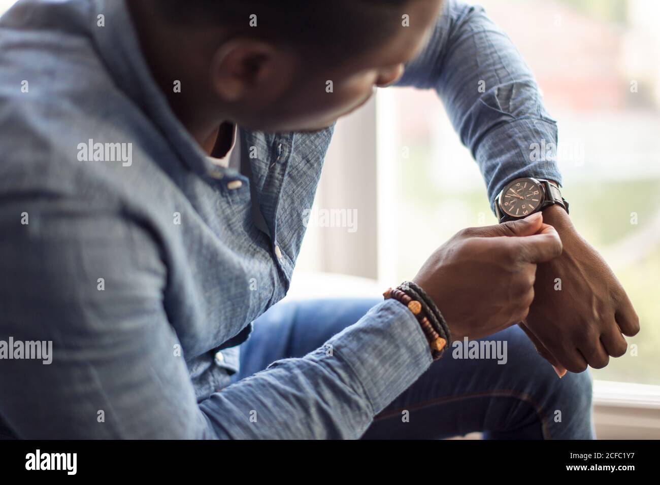 Handsome african man looking at his watch while sitting in his home or ...