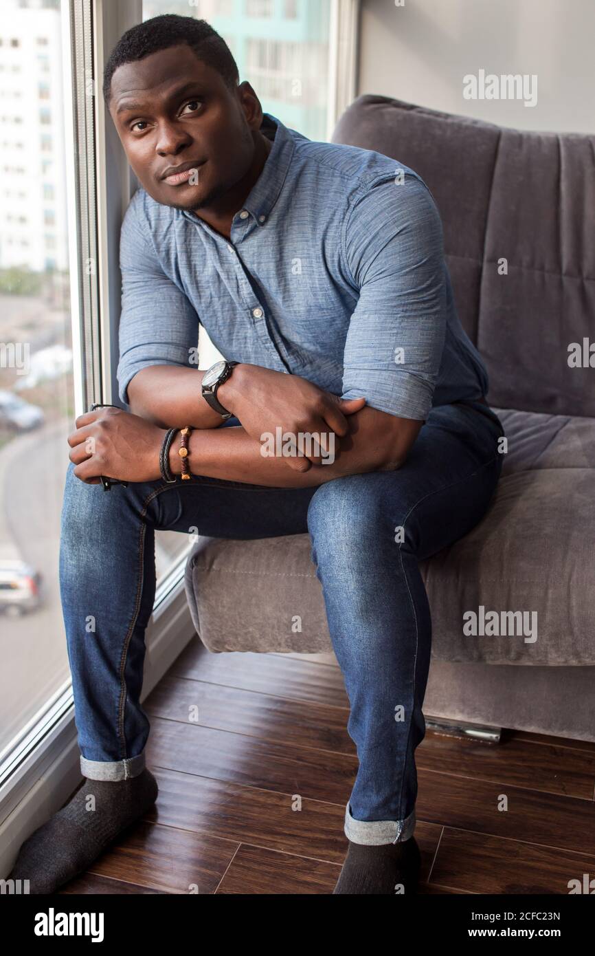 African man sitting on sofa and looking out the window Stock Photo - Alamy