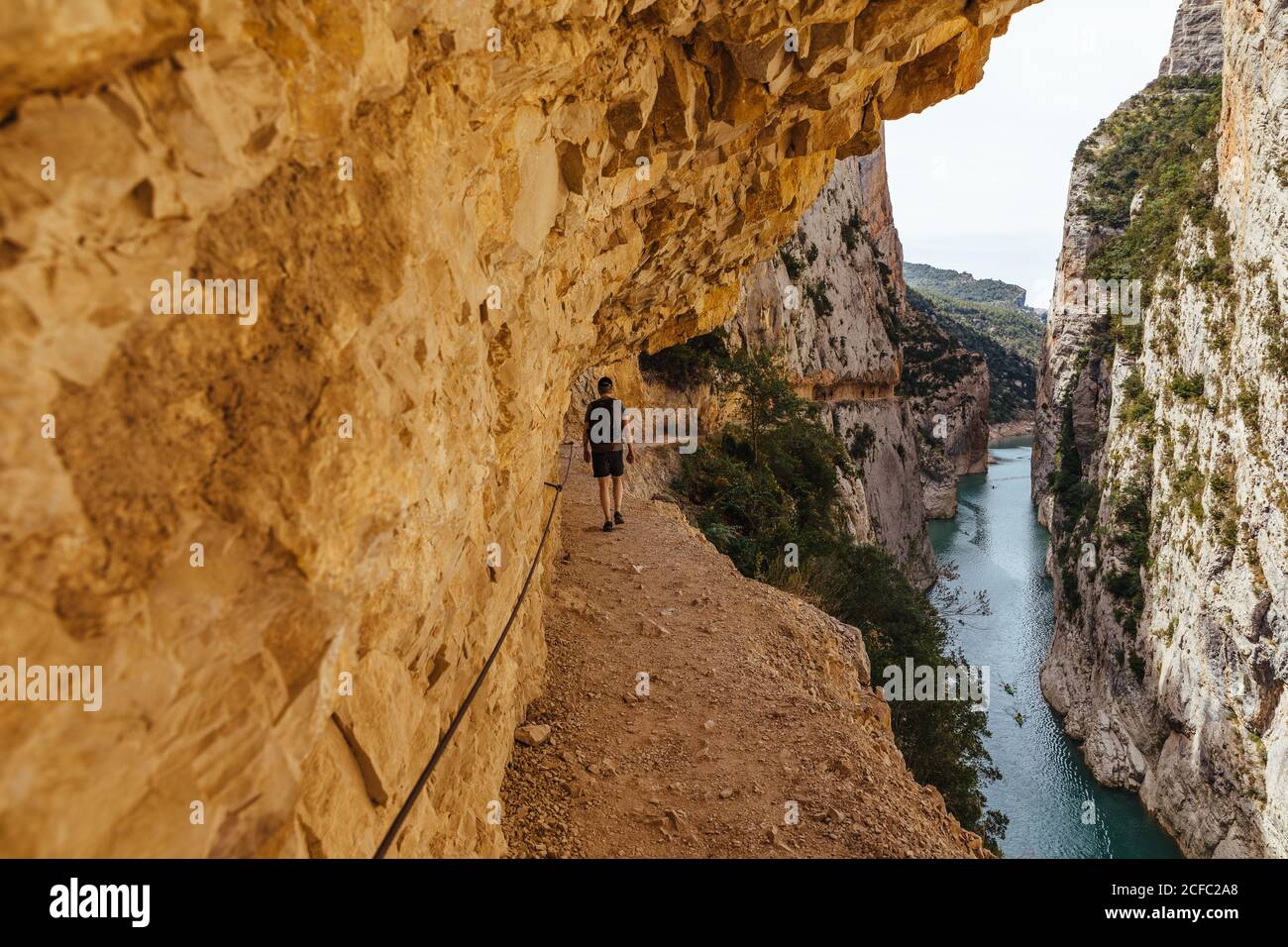 Back view of unrecognizable man hiking through a gorge close to a river ...