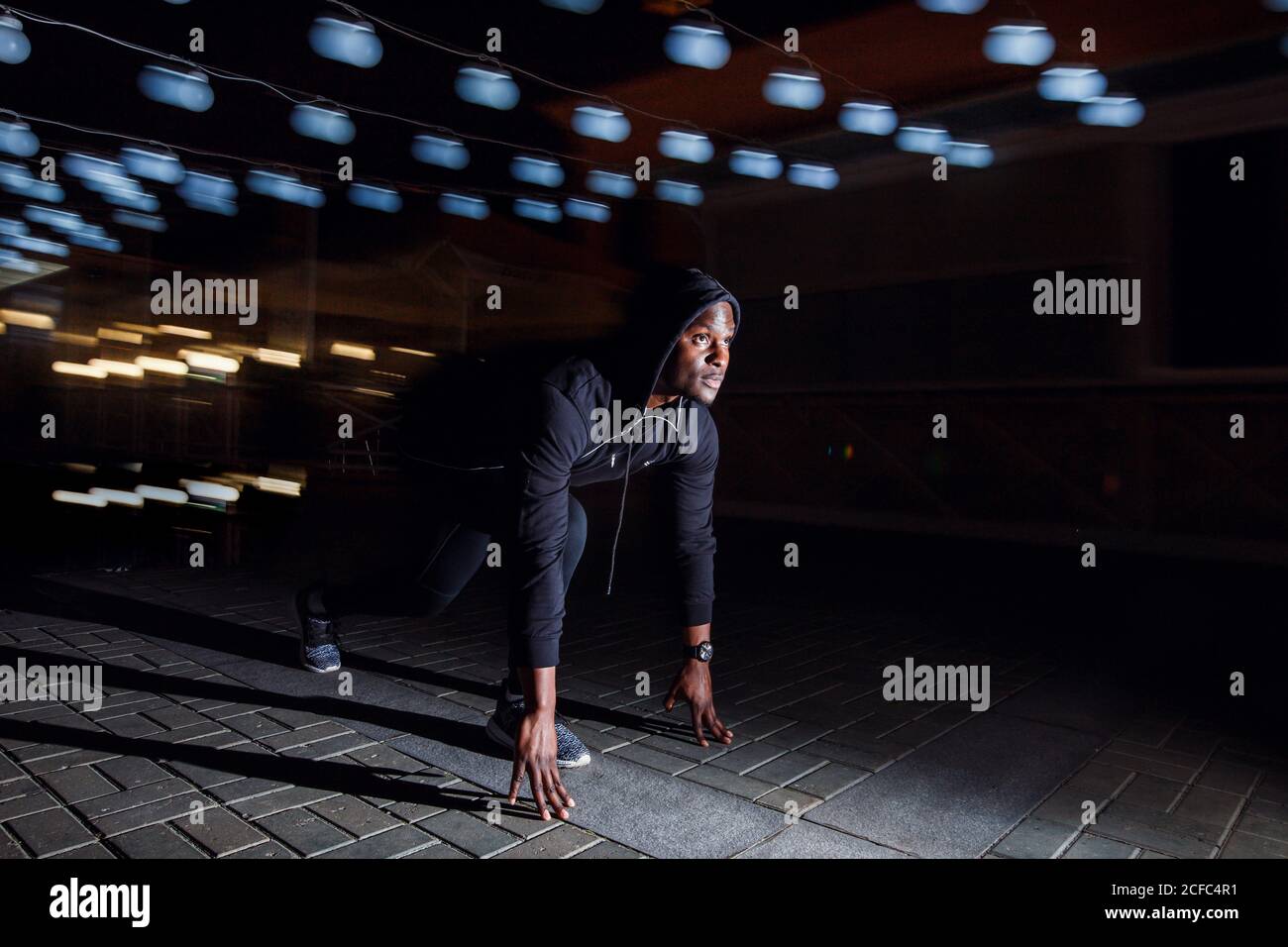 One young adult man, runner, sprinter, start position. Night time dark ...