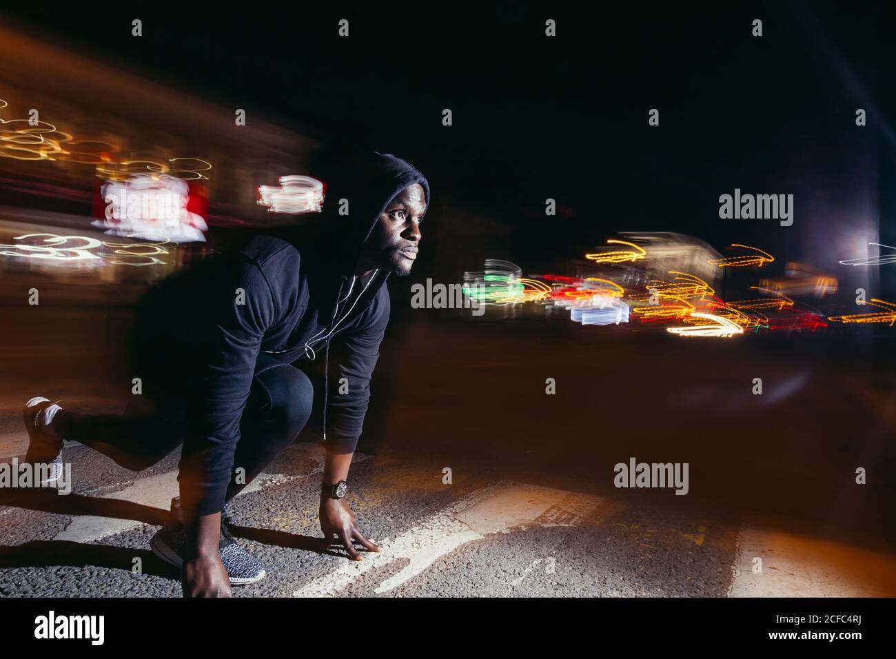 One young adult man, runner, sprinter, start position. Night time dark ...