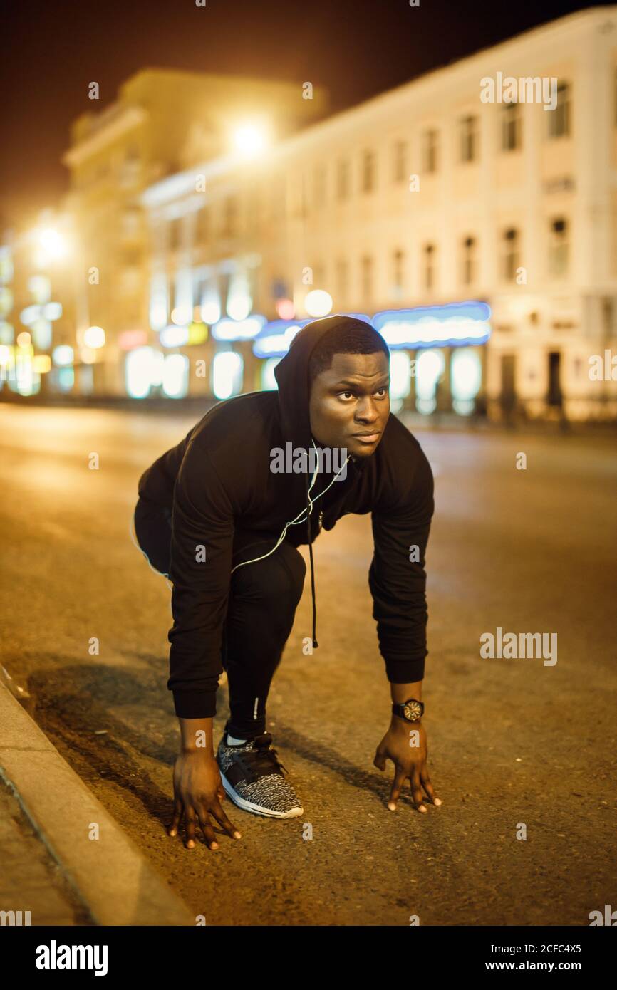 One young adult man, runner, sprinter, start position. Night time dark ...