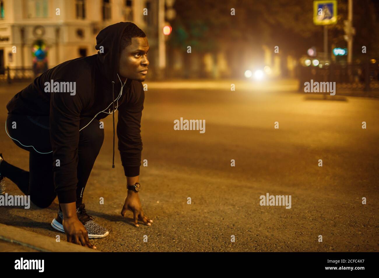 One young adult man, runner, sprinter, start position. Night time dark ...