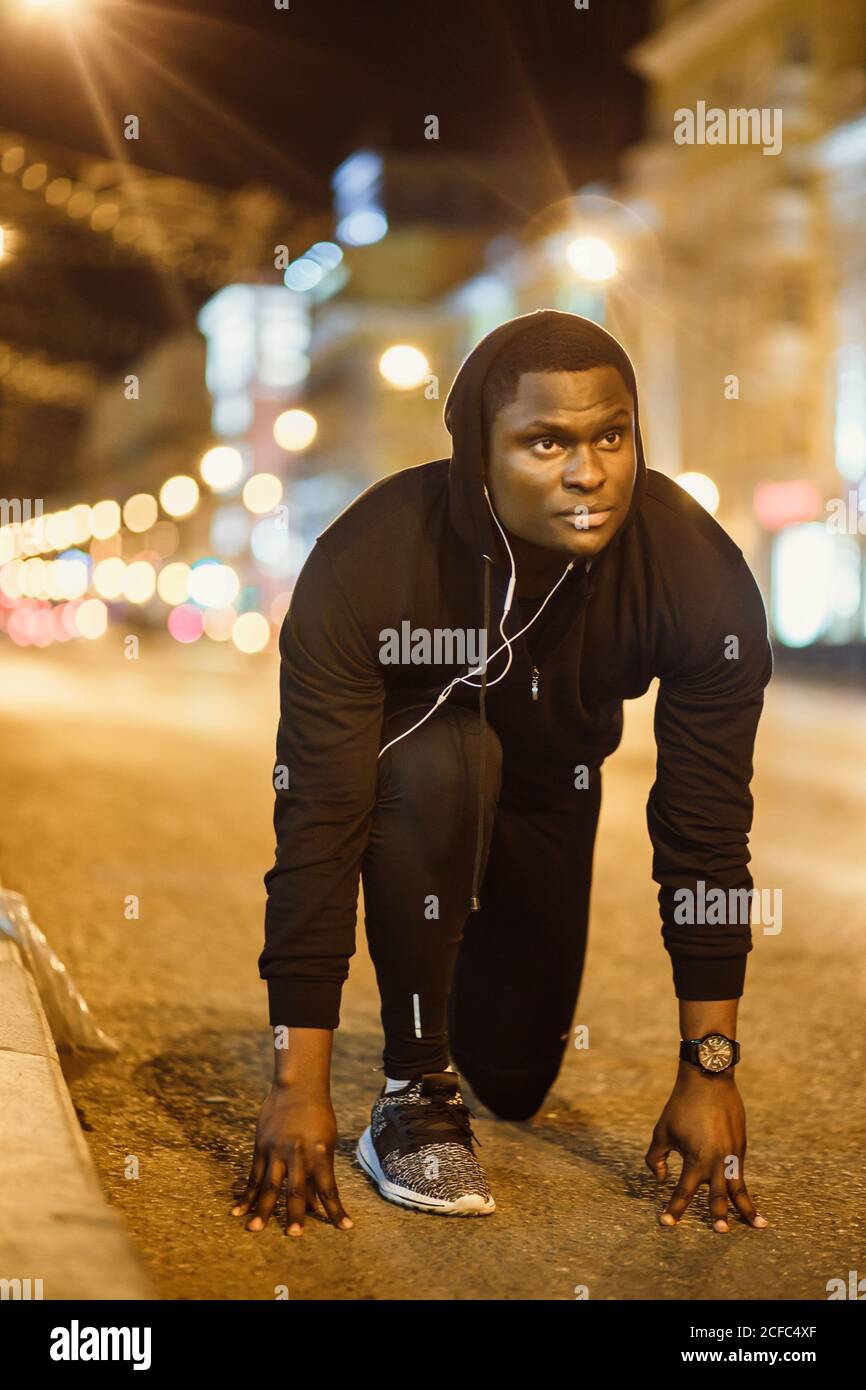 One young adult man, runner, sprinter, start position. Night time dark ...