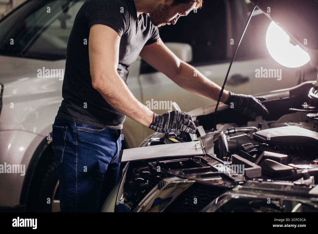 Mechanic perform vehicle checkup and make notes in notepad in garage ...