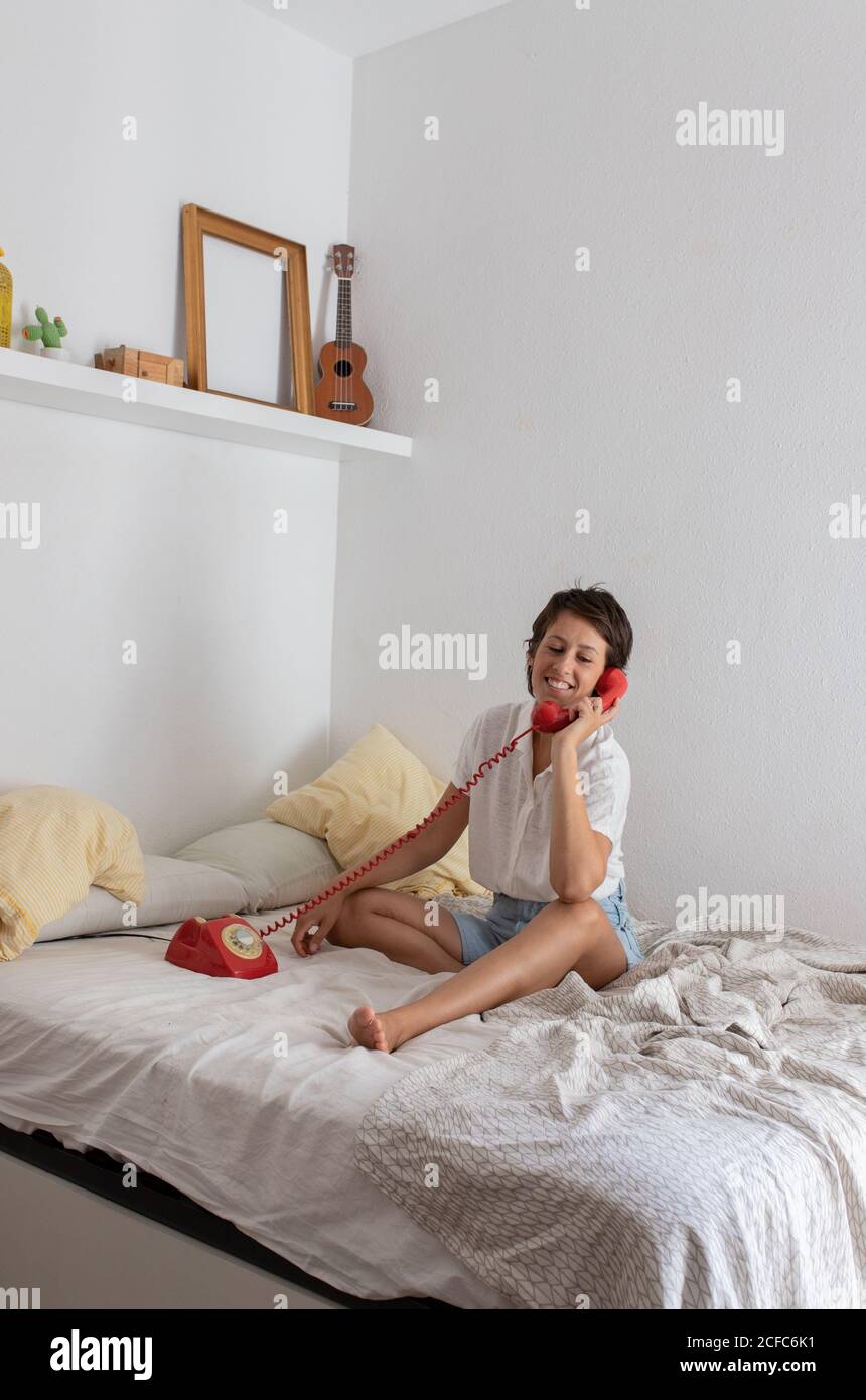 Pleased young female smiling and answering phone call from vintage red ...