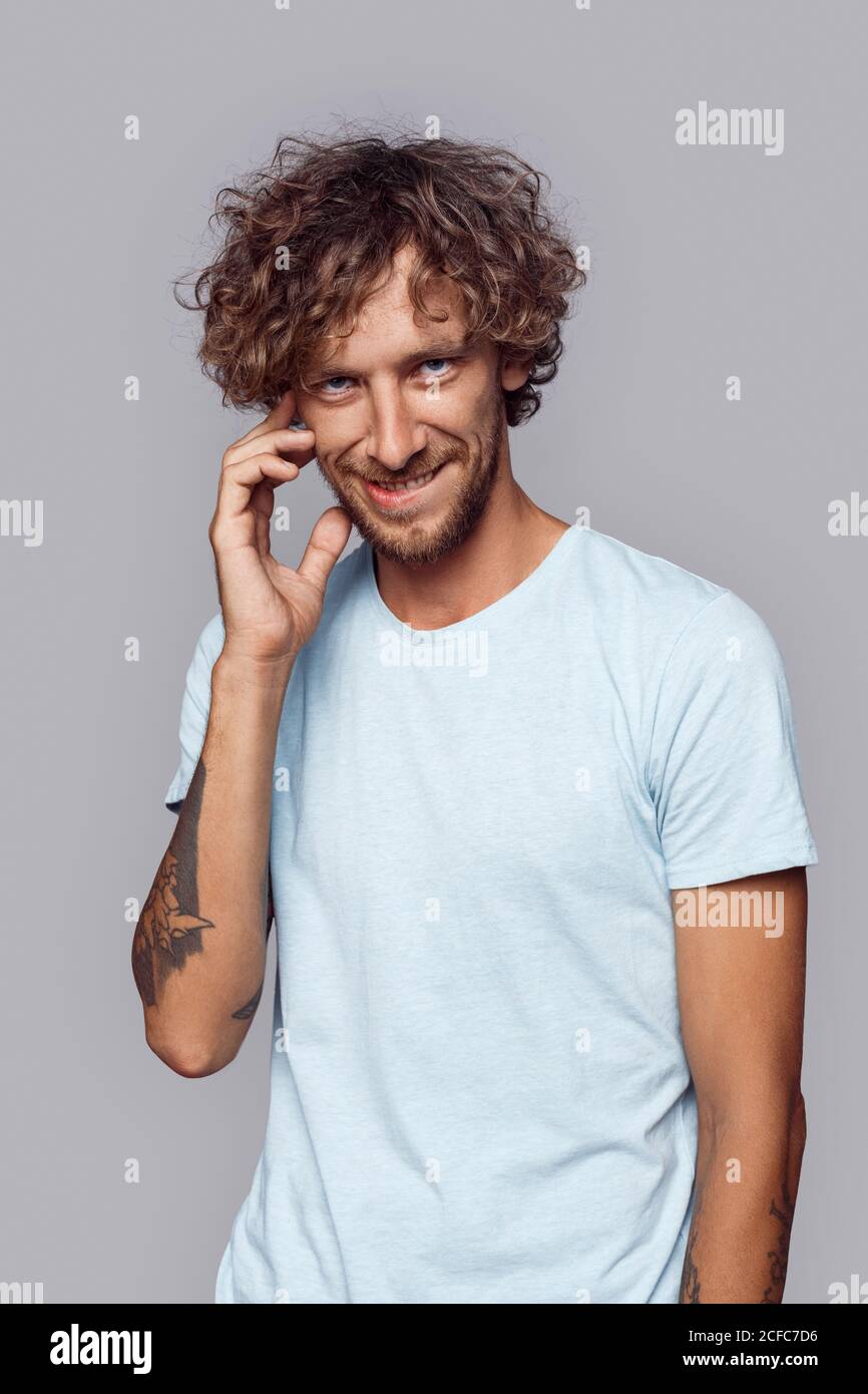 Freestyle. Man with curly hair in t-shirt standing isolated on grey ...