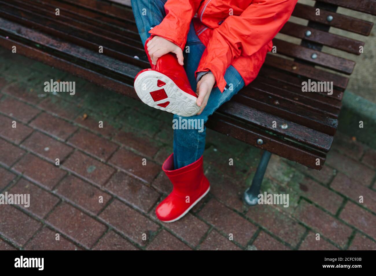 From above cropped unrecognizable wet kid in red raincoat and rubber ...