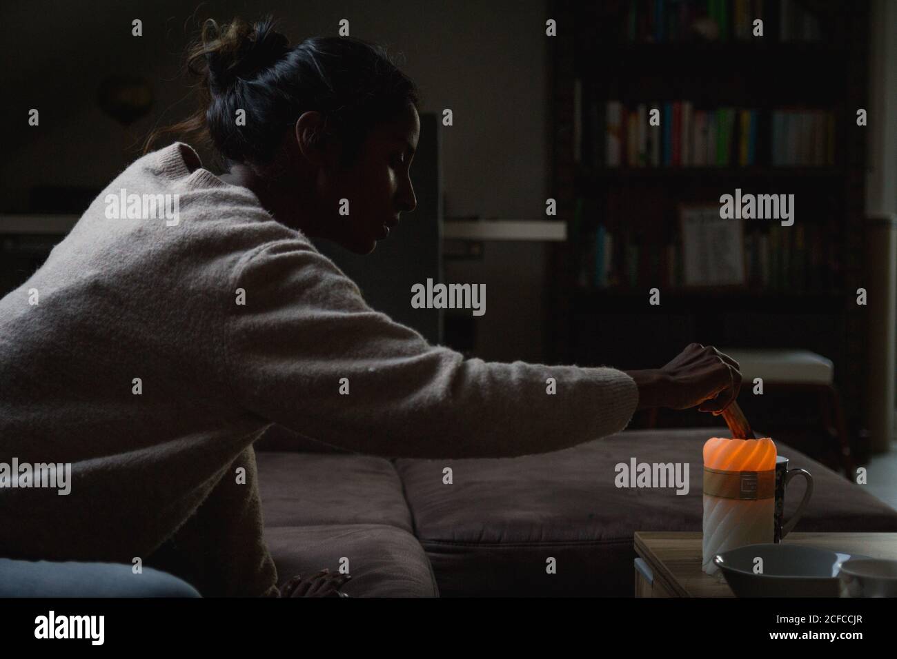 Side view of Indian female in cozy sweater sitting on soft couch in ...