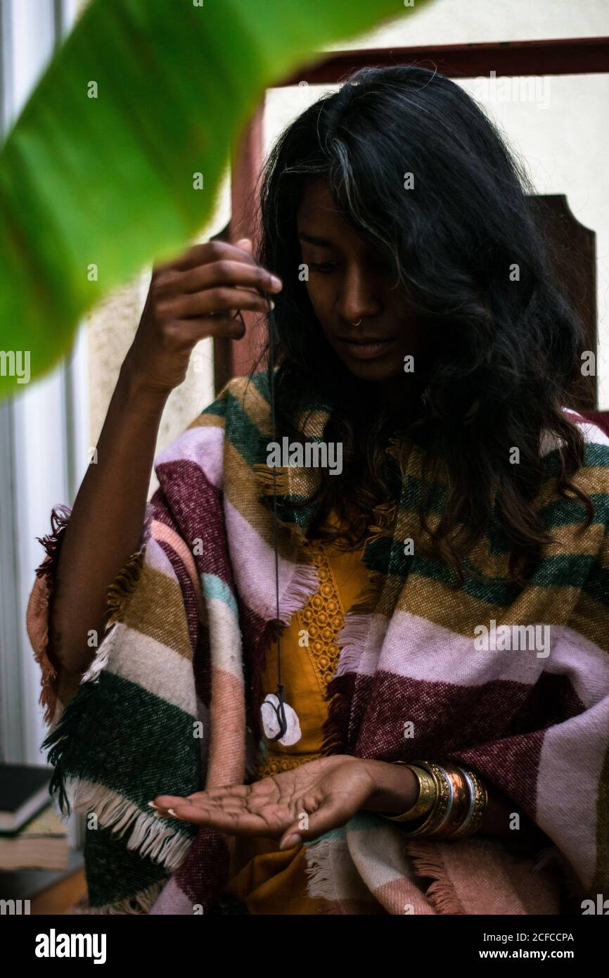 Young ethnic female shaman in traditional outfit holding pendant ...