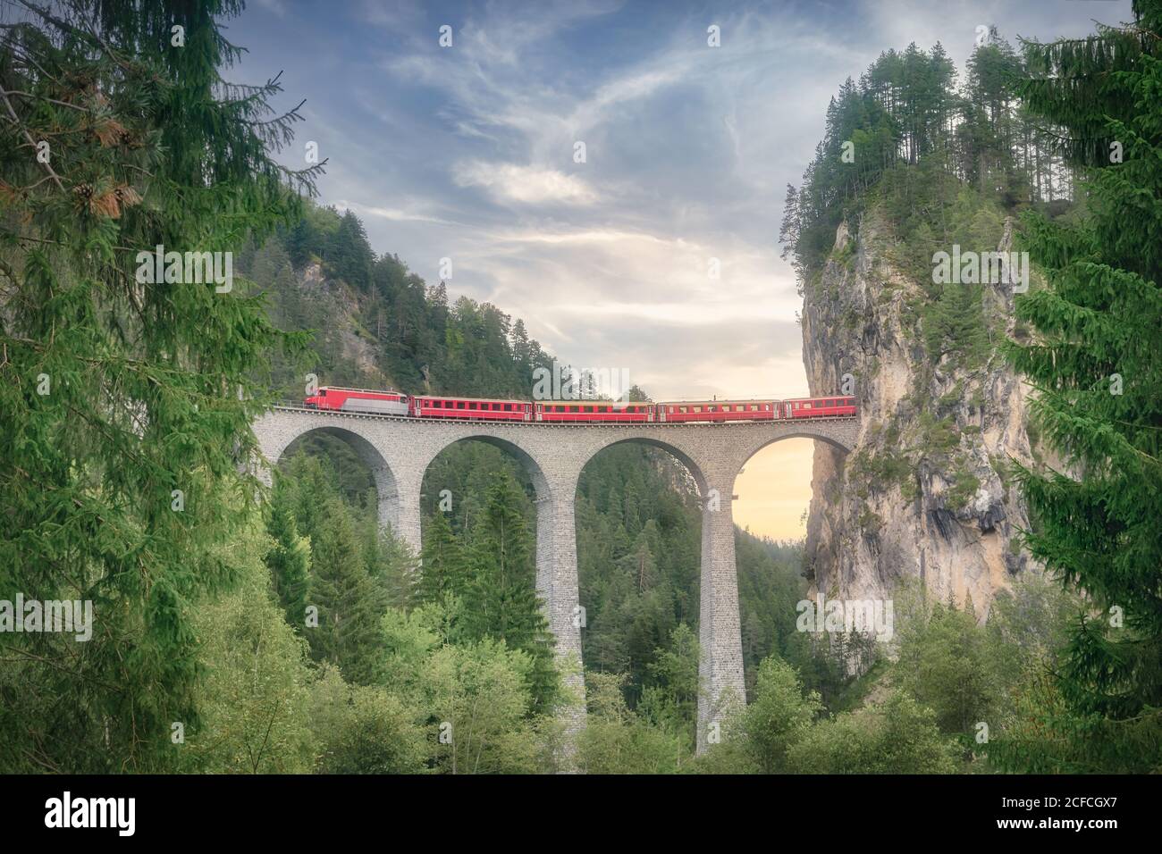 Picturesque view of red train passing high arched bridge from tunnel in ...