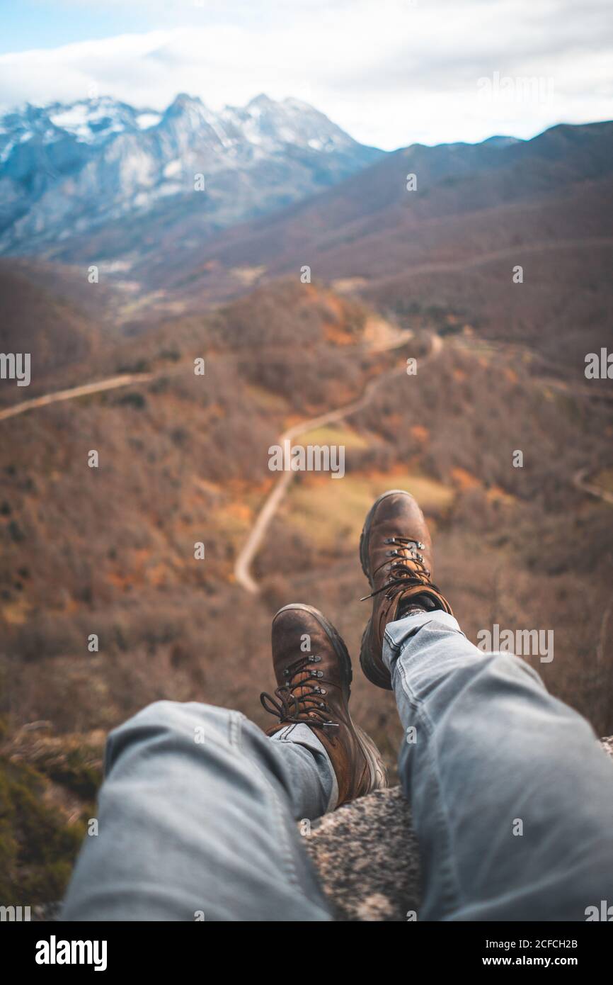 Crop traveler in brown boots sitting with legs dangling on edge on rock ...