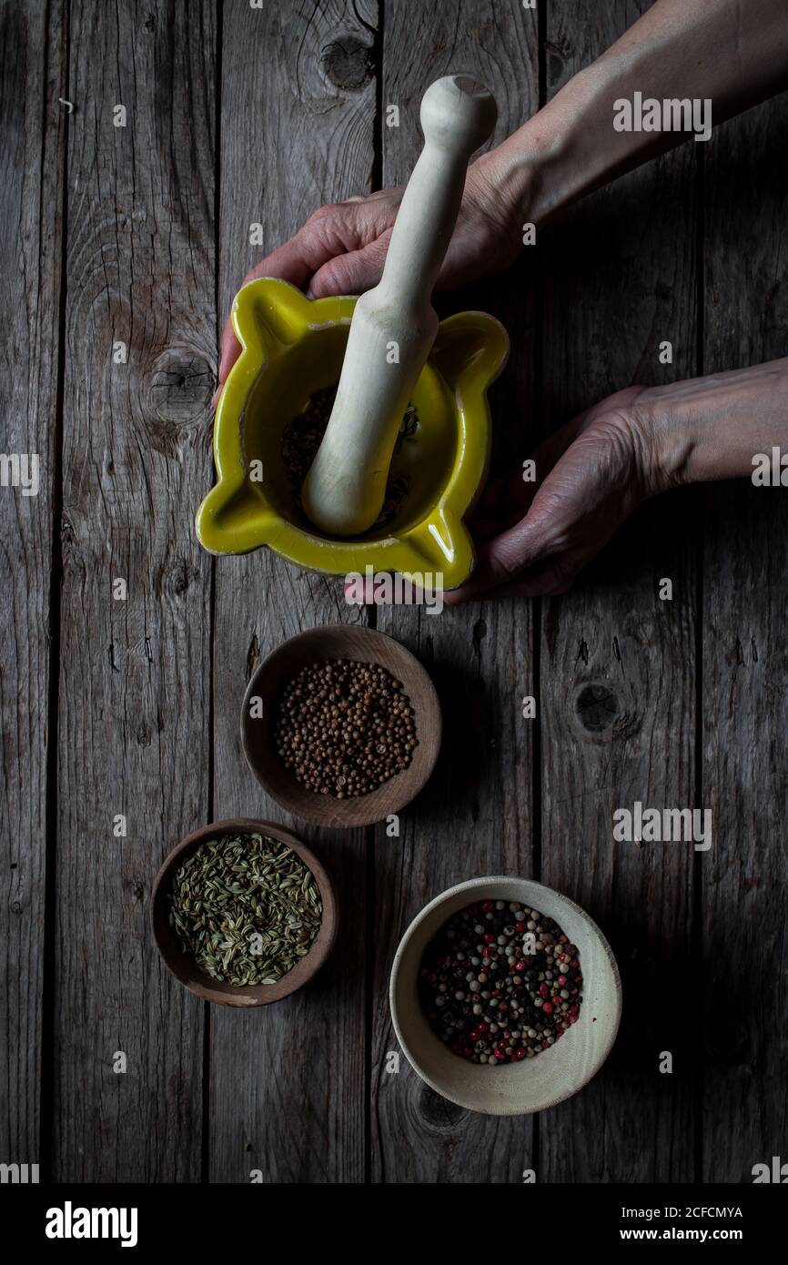 Crop view from above of cook grounding spices in mortar while cooking ...