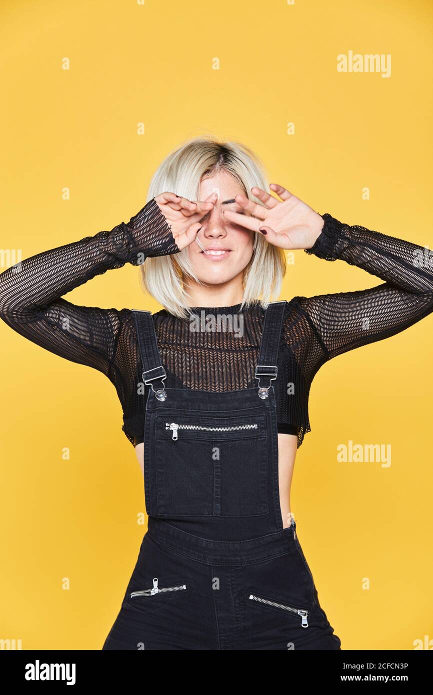 Attractive blonde Woman in black overalls standing and covering eyes ...